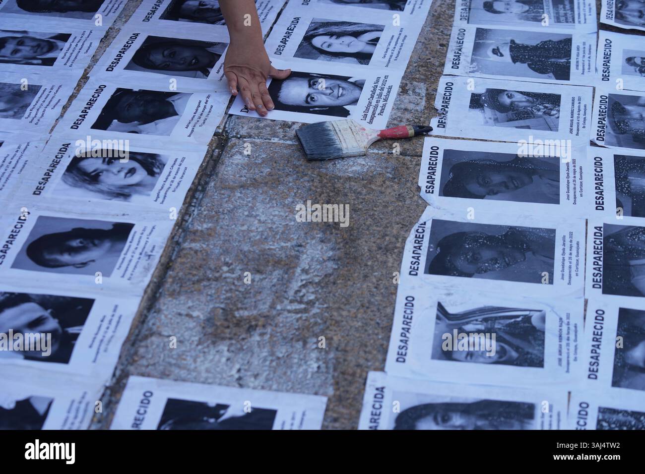 Protesters line a sidewalk with images of missing persons, outside a ...