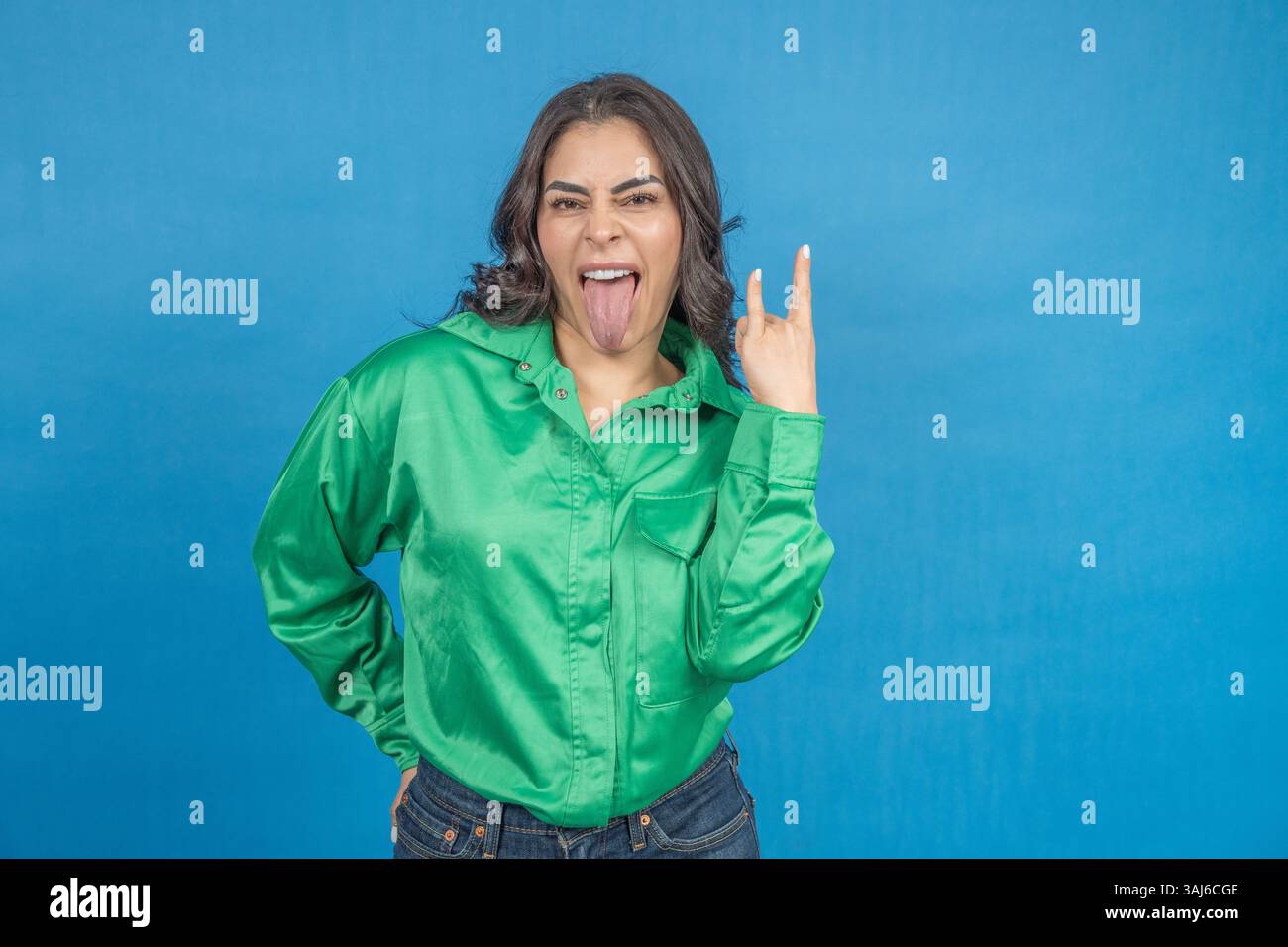 Playful young woman sticking out her tongue and making the rock and roll hand sign against a ...