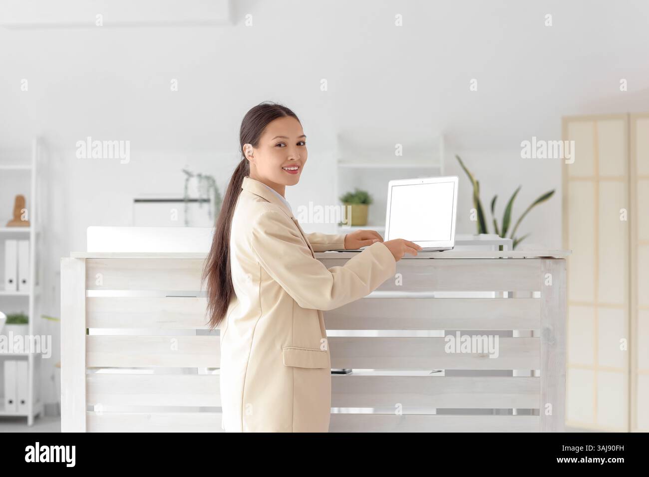 Young female receptionist working with modern laptop at reception desk ...