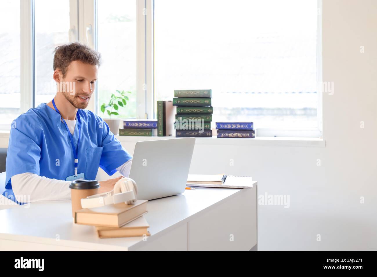 Male medical intern studying with laptop at table in library Stock ...