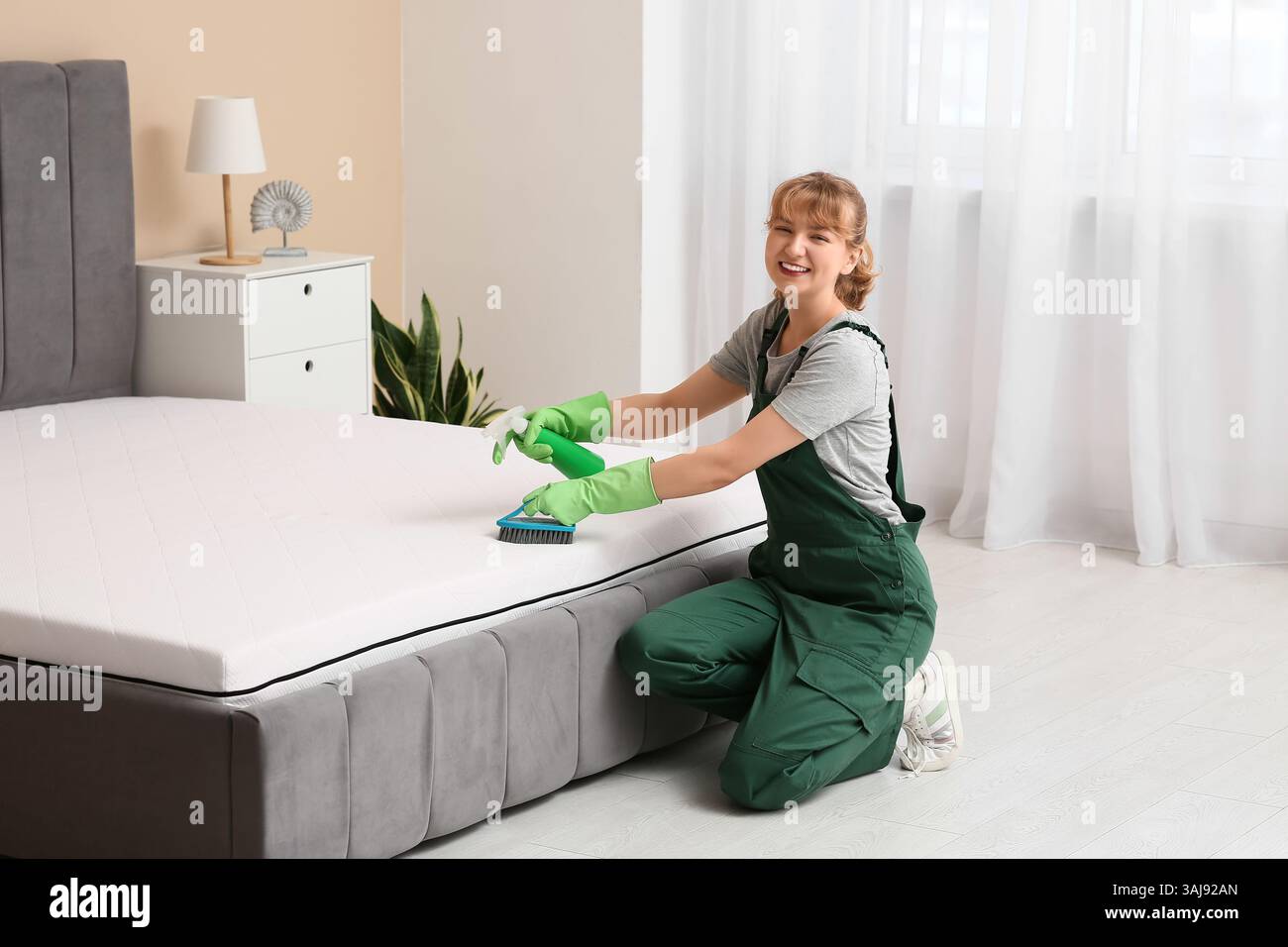 Female janitor cleaning mattress with brush and detergent in bedroom ...