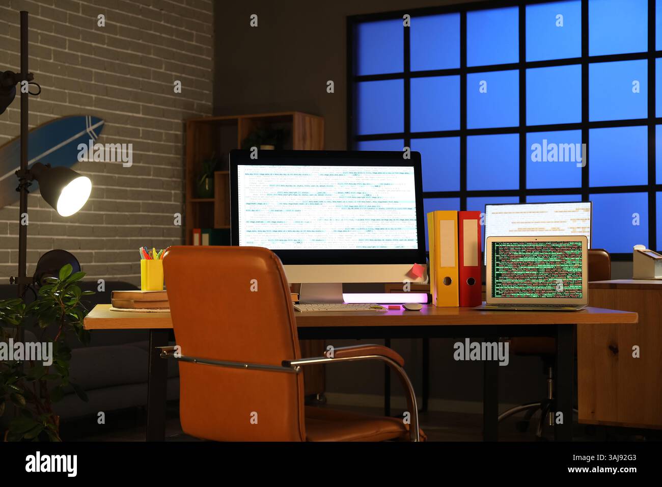 Computer monitor and laptop with codes on programmer's desk in dark ...