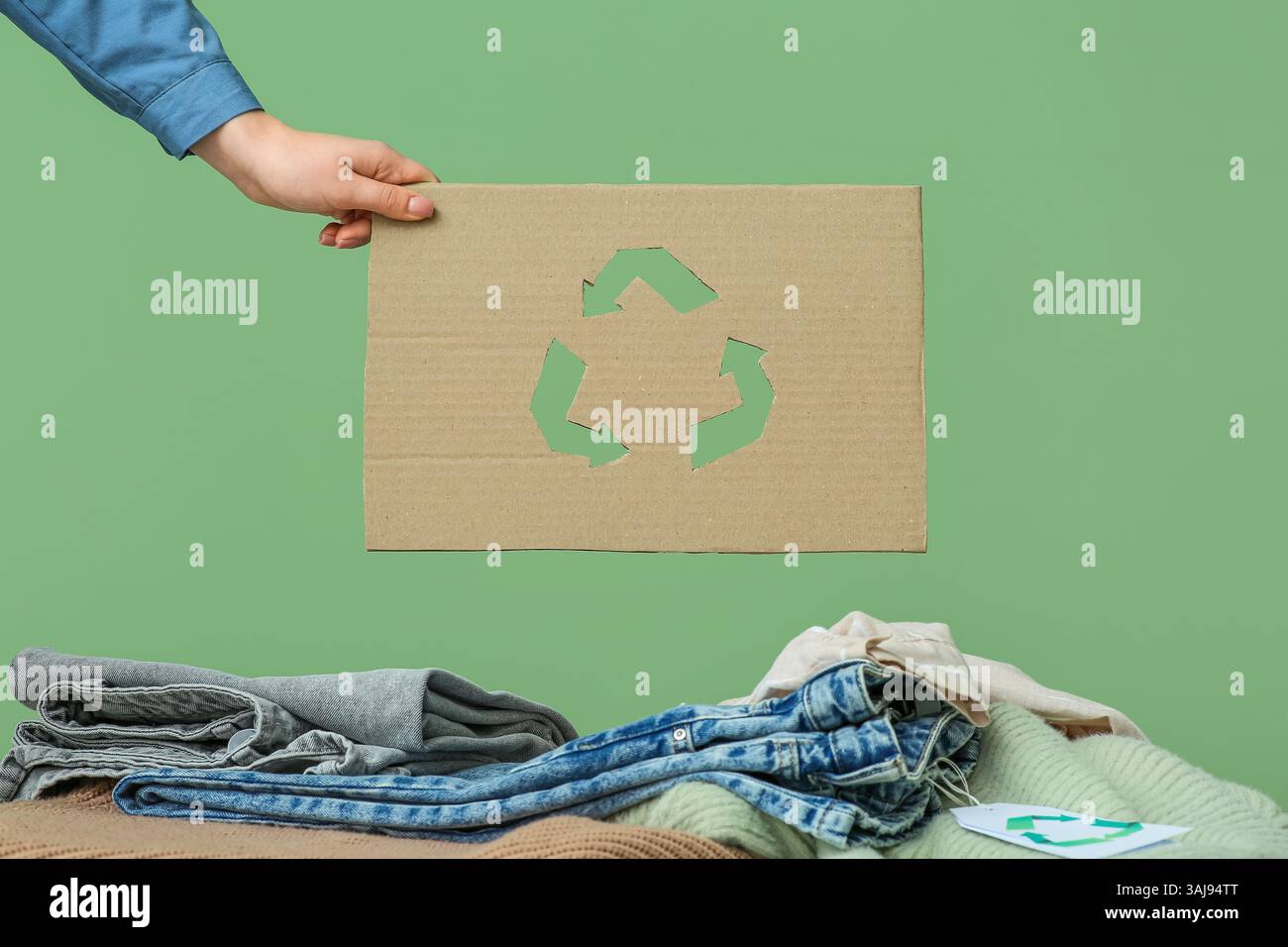 Woman holding sign with recycling logo above clothes on green ...