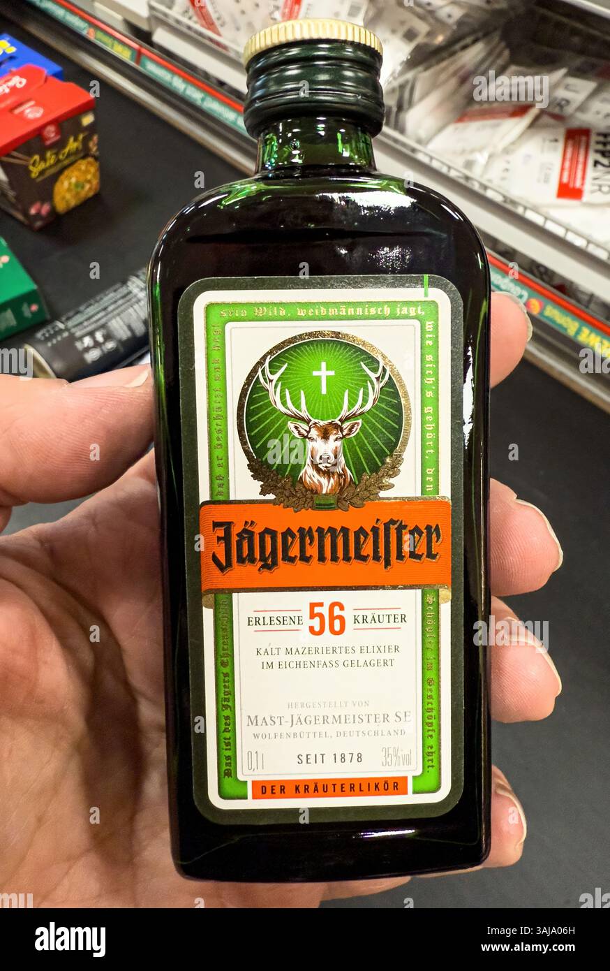 Hand holding a small bottle of jagermeister liqueur in a supermarket ...