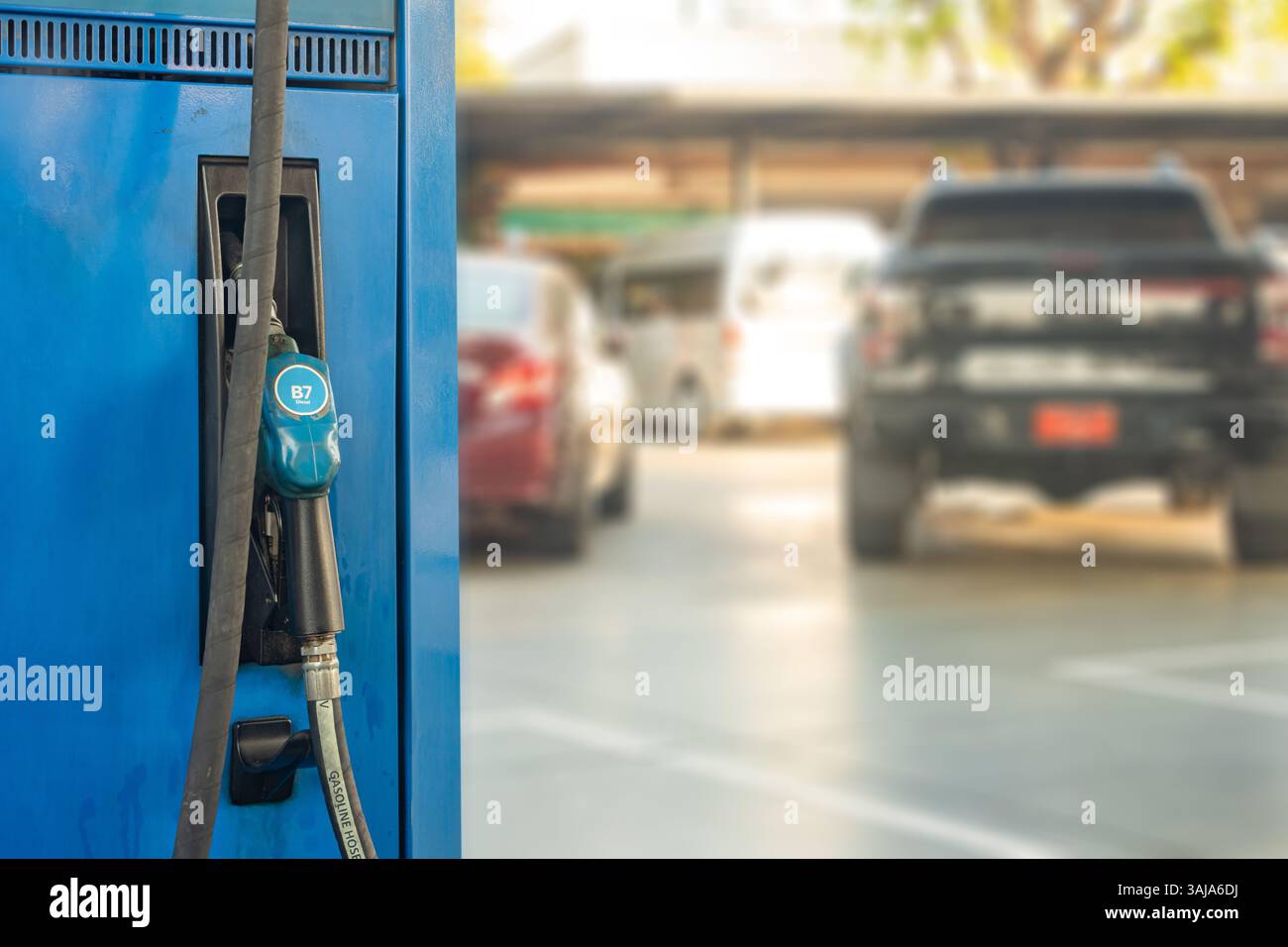 Fuel pump stand with pistol - nozzle, vehicles parking at background ...