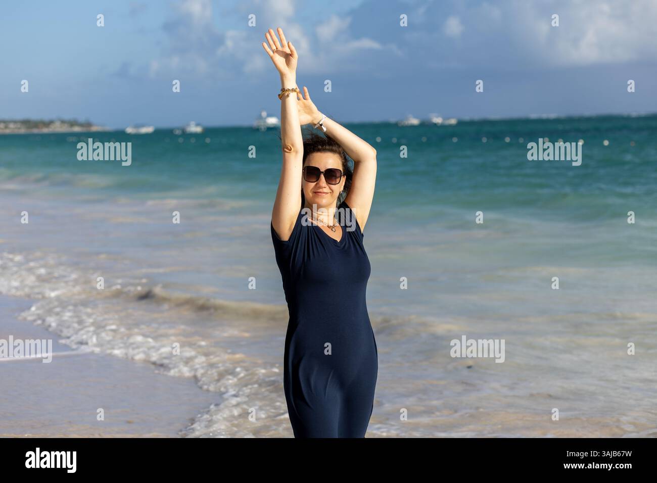 A woman stands on the sandy beach, arms raised, celebrating the ...