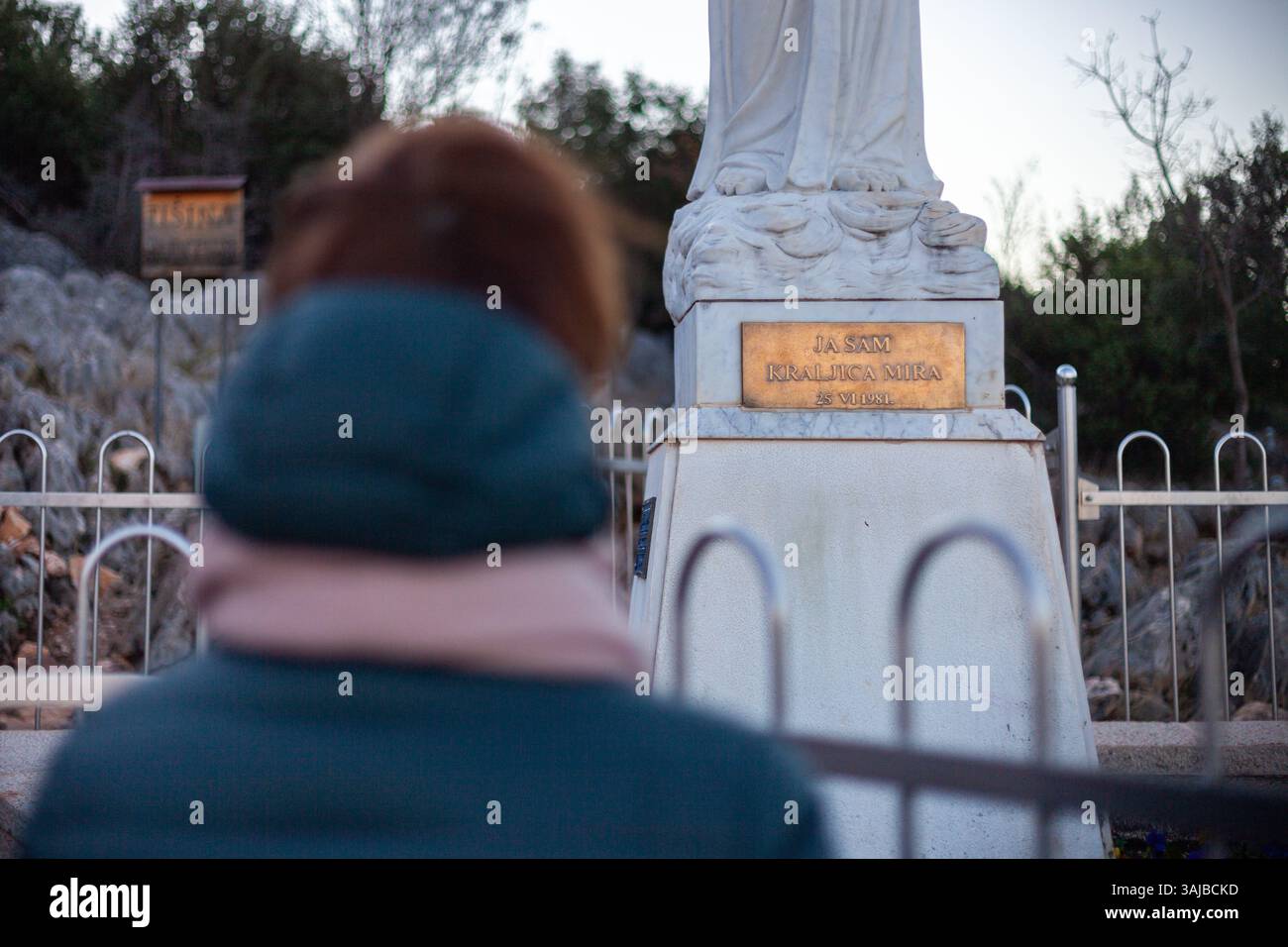 A woman praying at the statue of the Virgin Mary, the Queen of Peace on ...