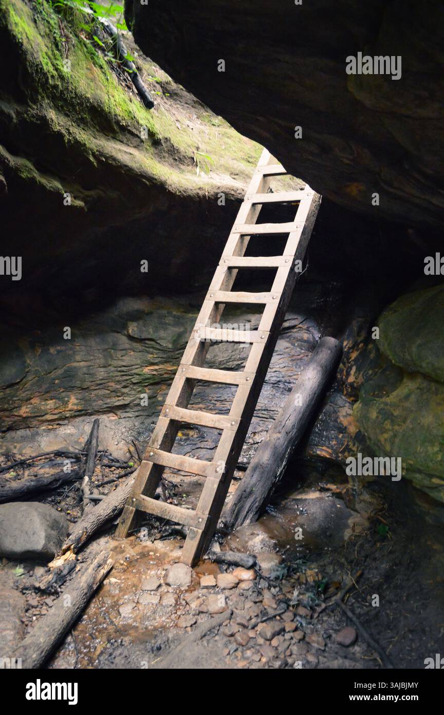 Wood ladder going up from a rocky stream bed through a narrow hole in a ...