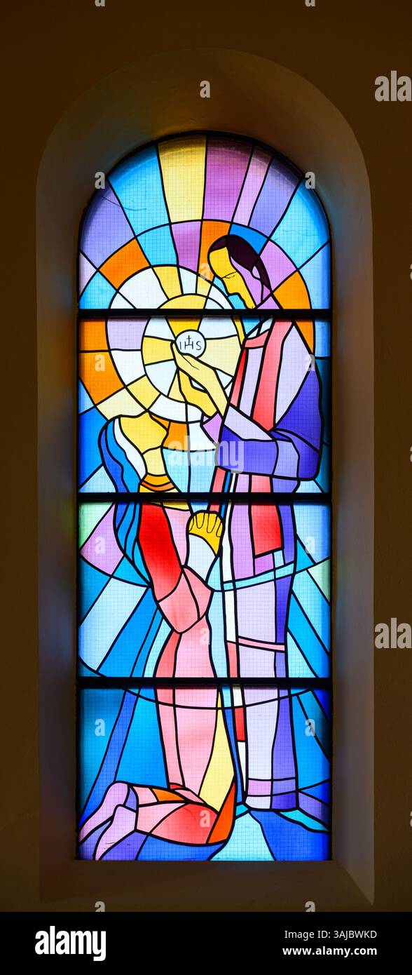 A priest giving the Eucharist to a kneeling young woman. A stained ...