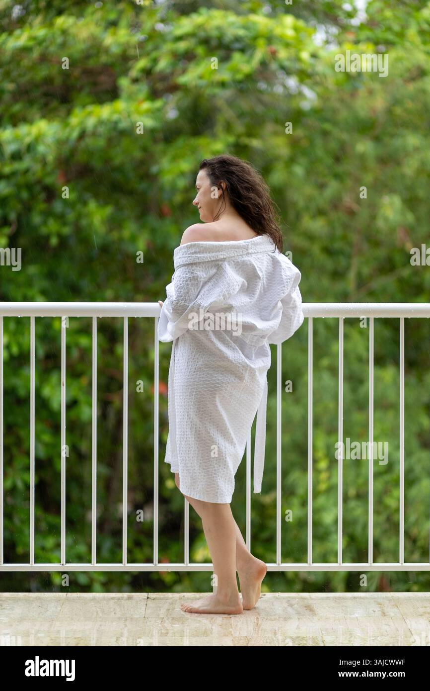 A woman stands on a balcony, gazing thoughtfully into the distance. She ...