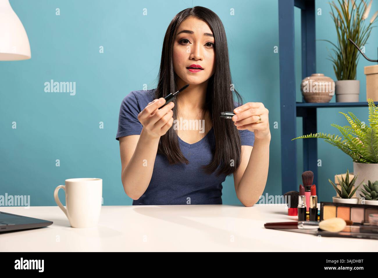 Young makeup artist holding a mascara, filming a tutorial for her online viewers. Asian female ...