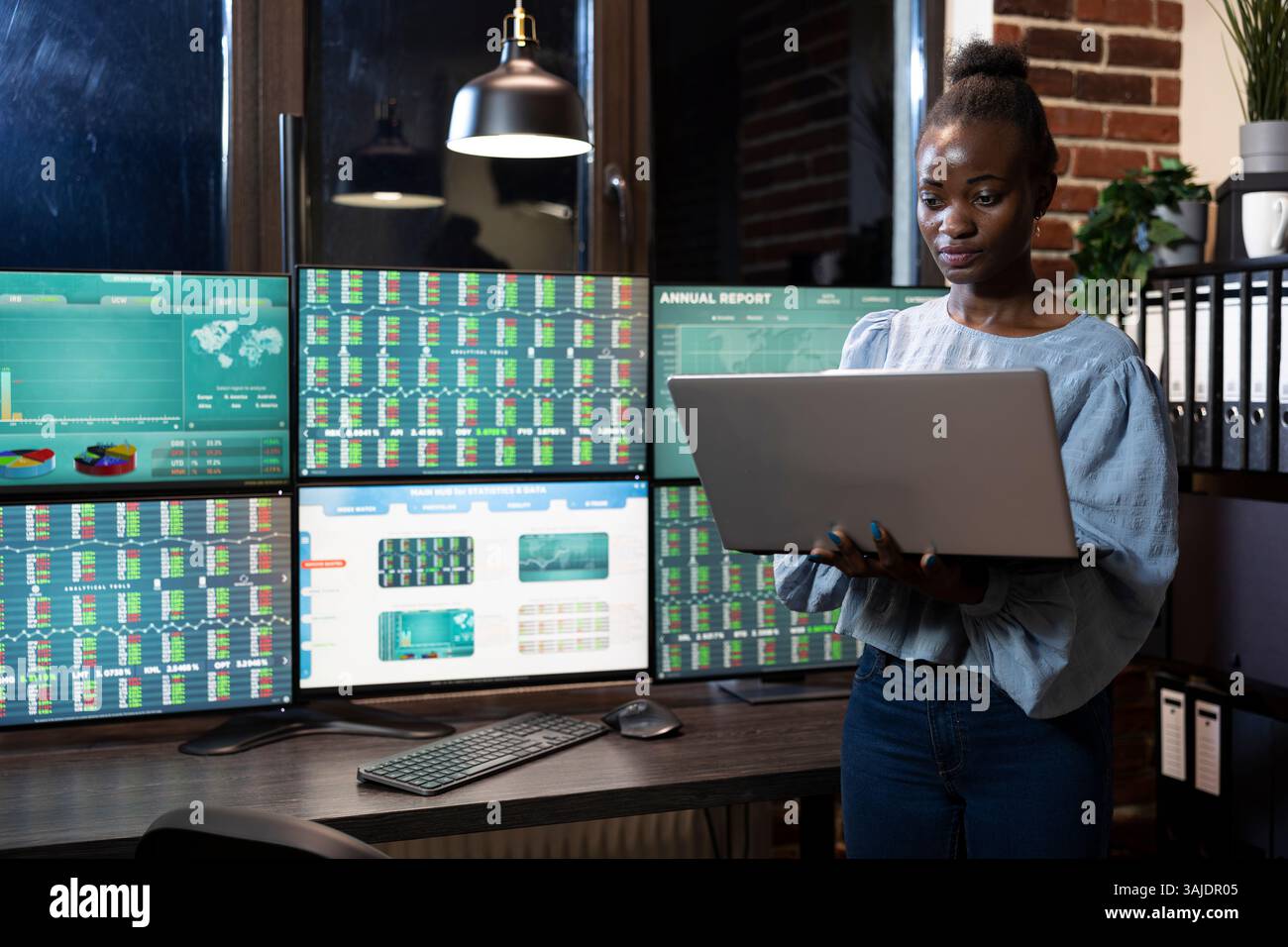 African American professional using her laptop, focuses on researching trading strategies. Young ...