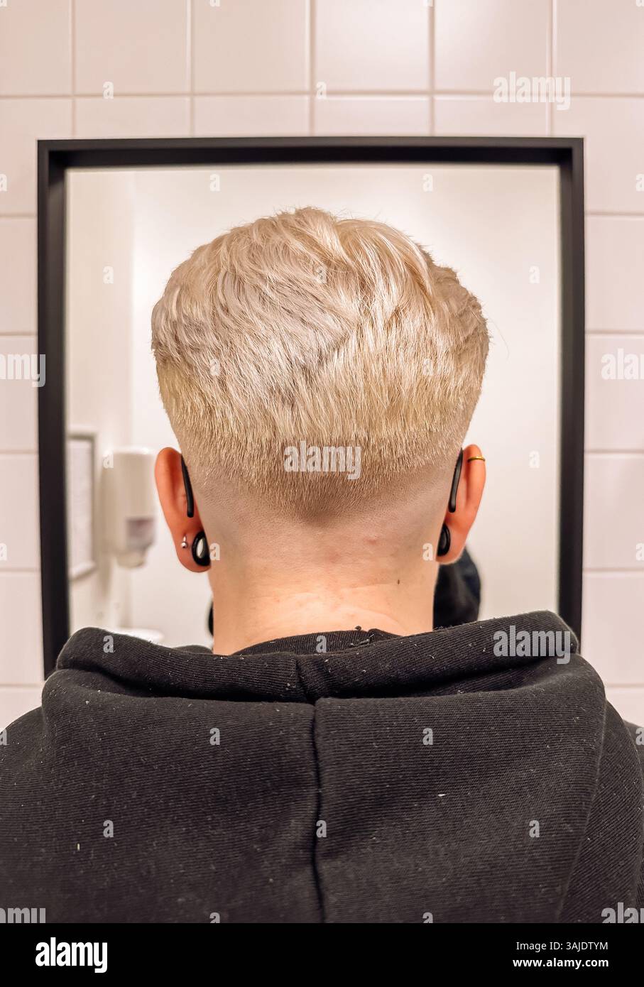 Man with a shaved head and a black hoodie is looking at himself in a ...