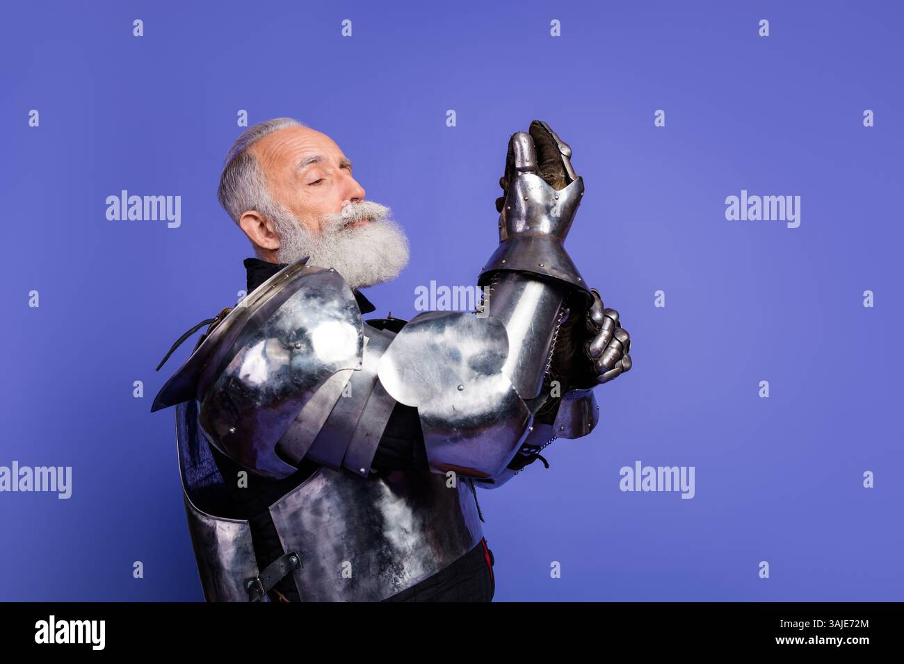 Elderly man in medieval knight's armor posing against violet background ...