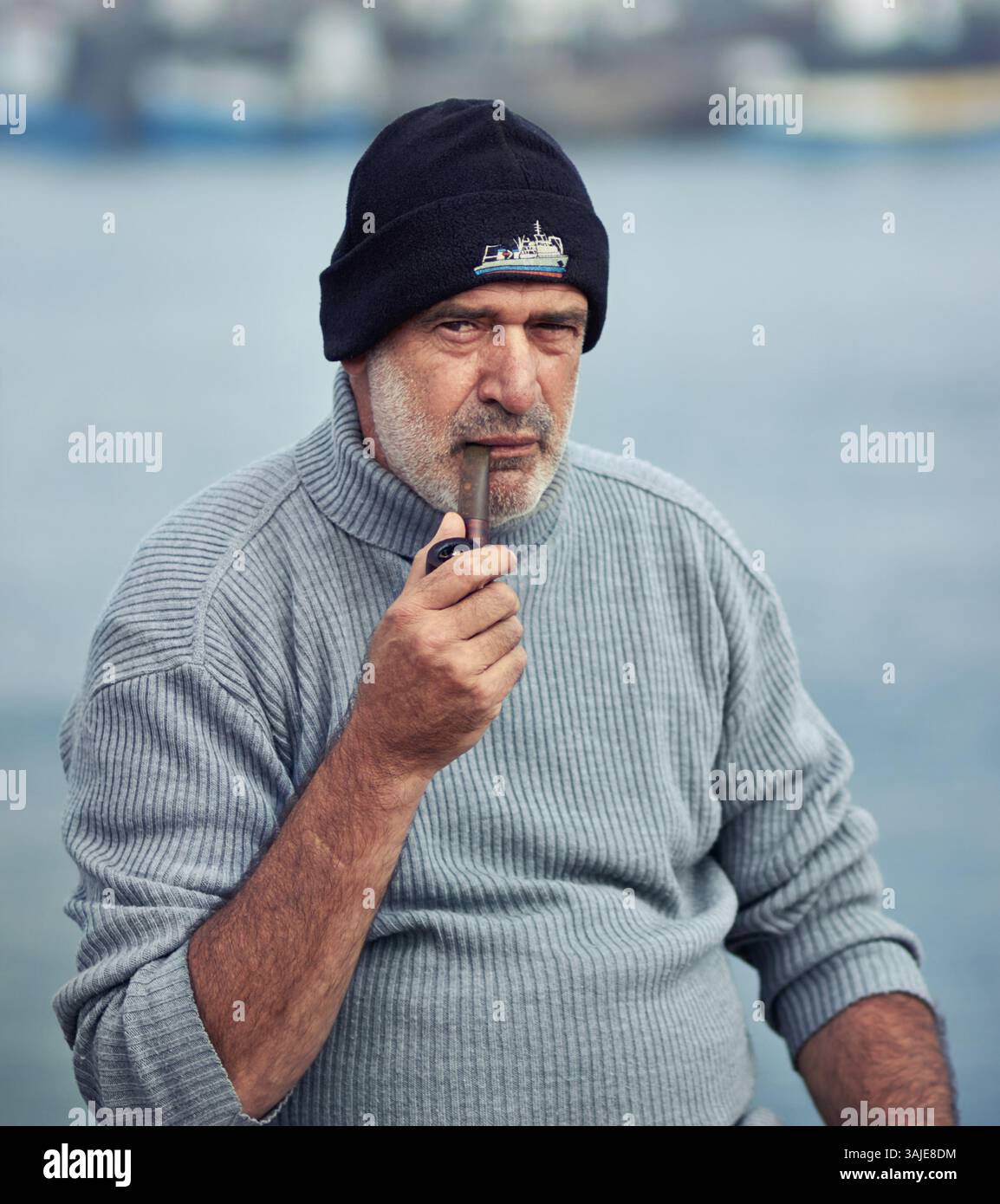 Fisherman portrait, serious man and smoking pipe by the sea water at a ...
