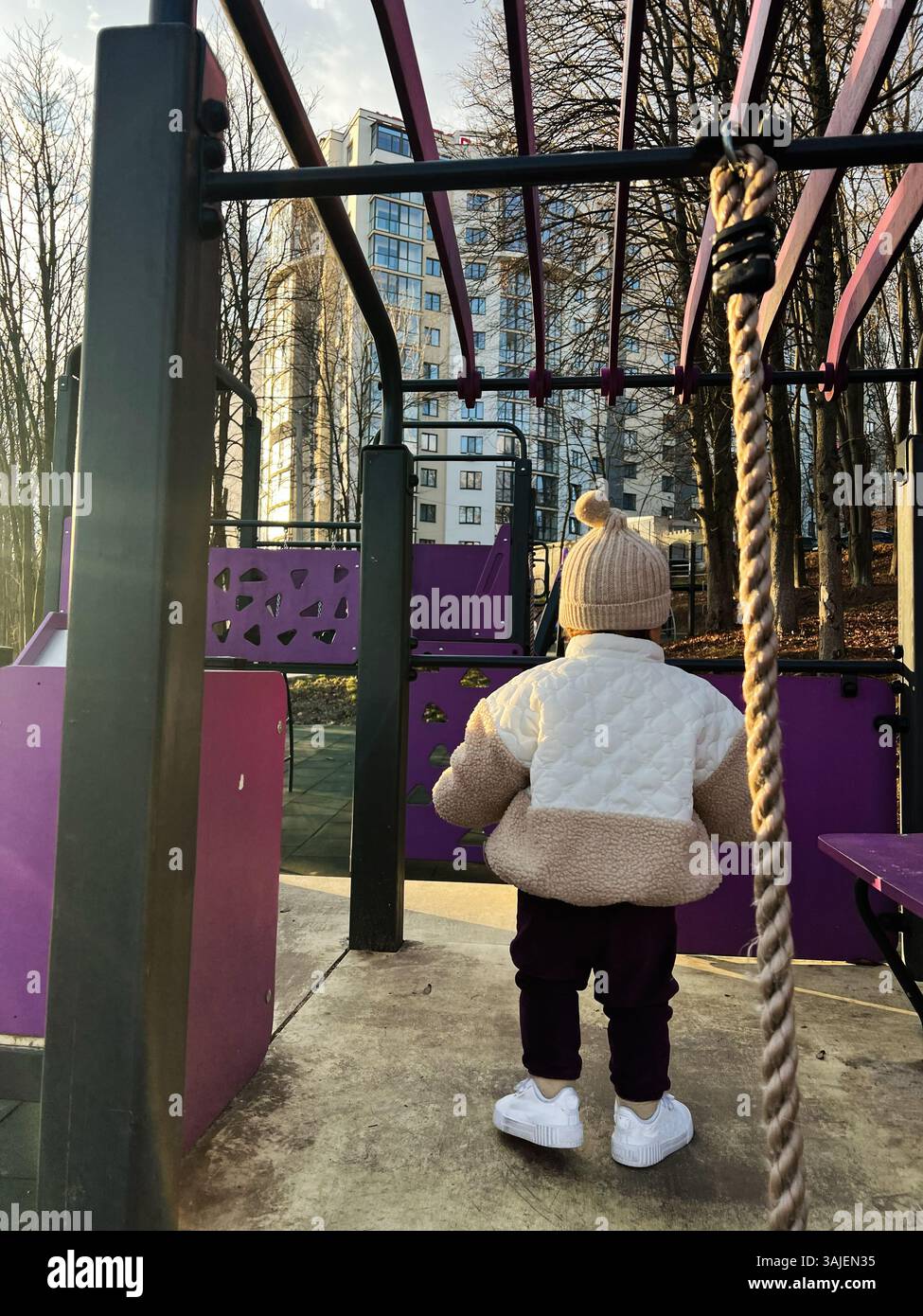 Child standing in a vibrant playground, wearing winter clothes, near ...