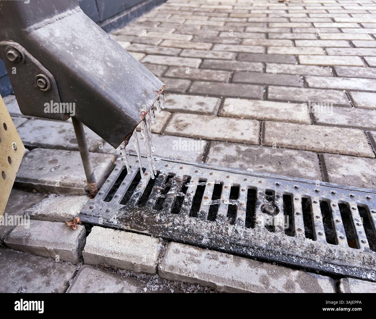 Water frozen into icicles drips from an outdoor pipe onto a metal drain ...