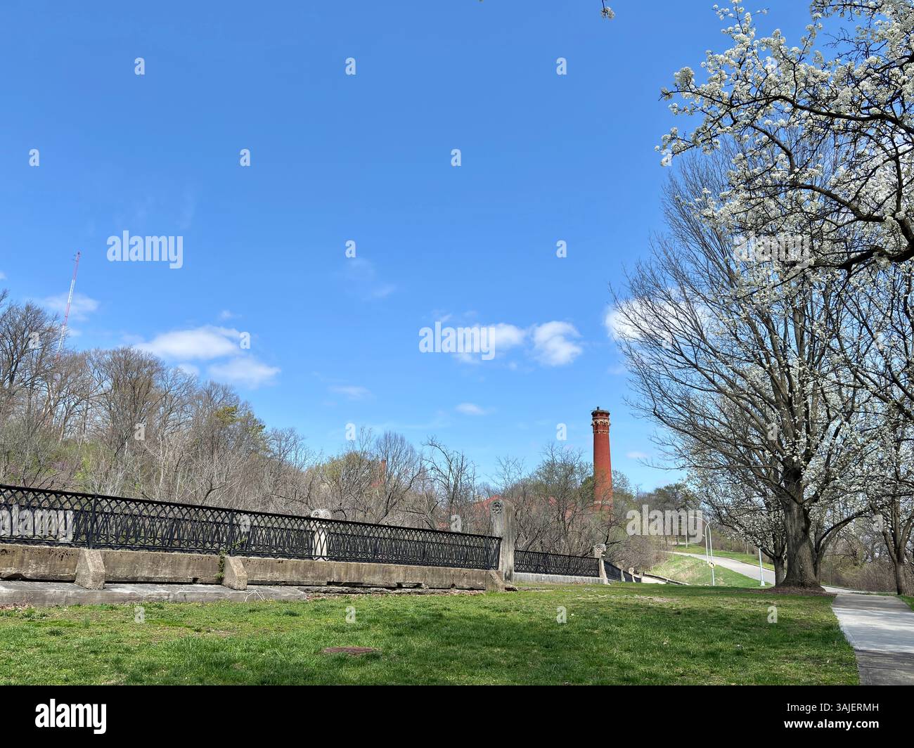 Blooming tree and iron bridge rail near tall red brick smokestack Stock ...