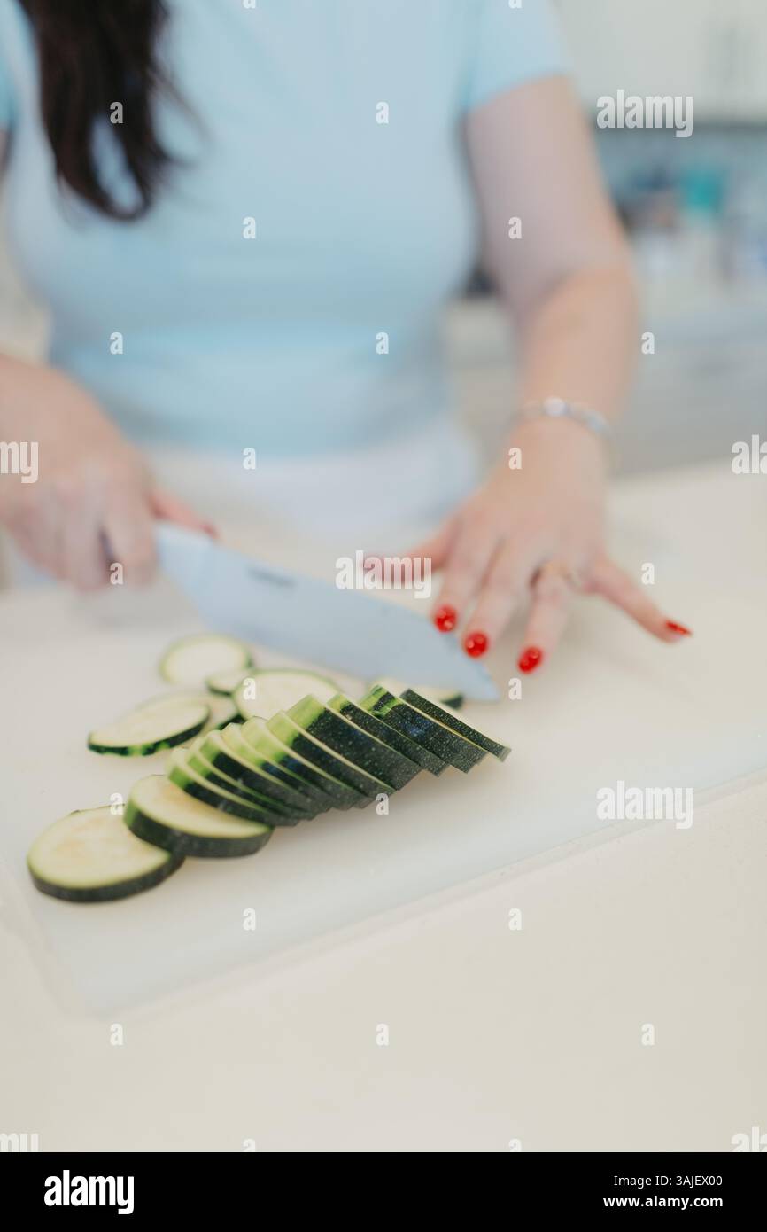 Woman slicing zucchini on white cutting board in kitchen Stock Photo ...