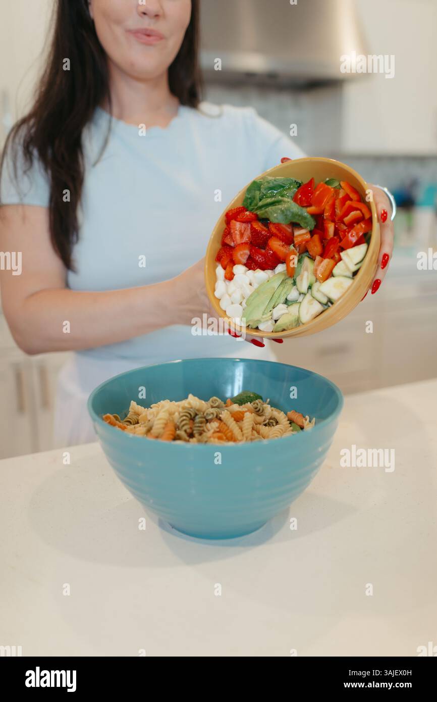 Woman adding fresh toppings to colorful pasta salad bowl Stock Photo ...