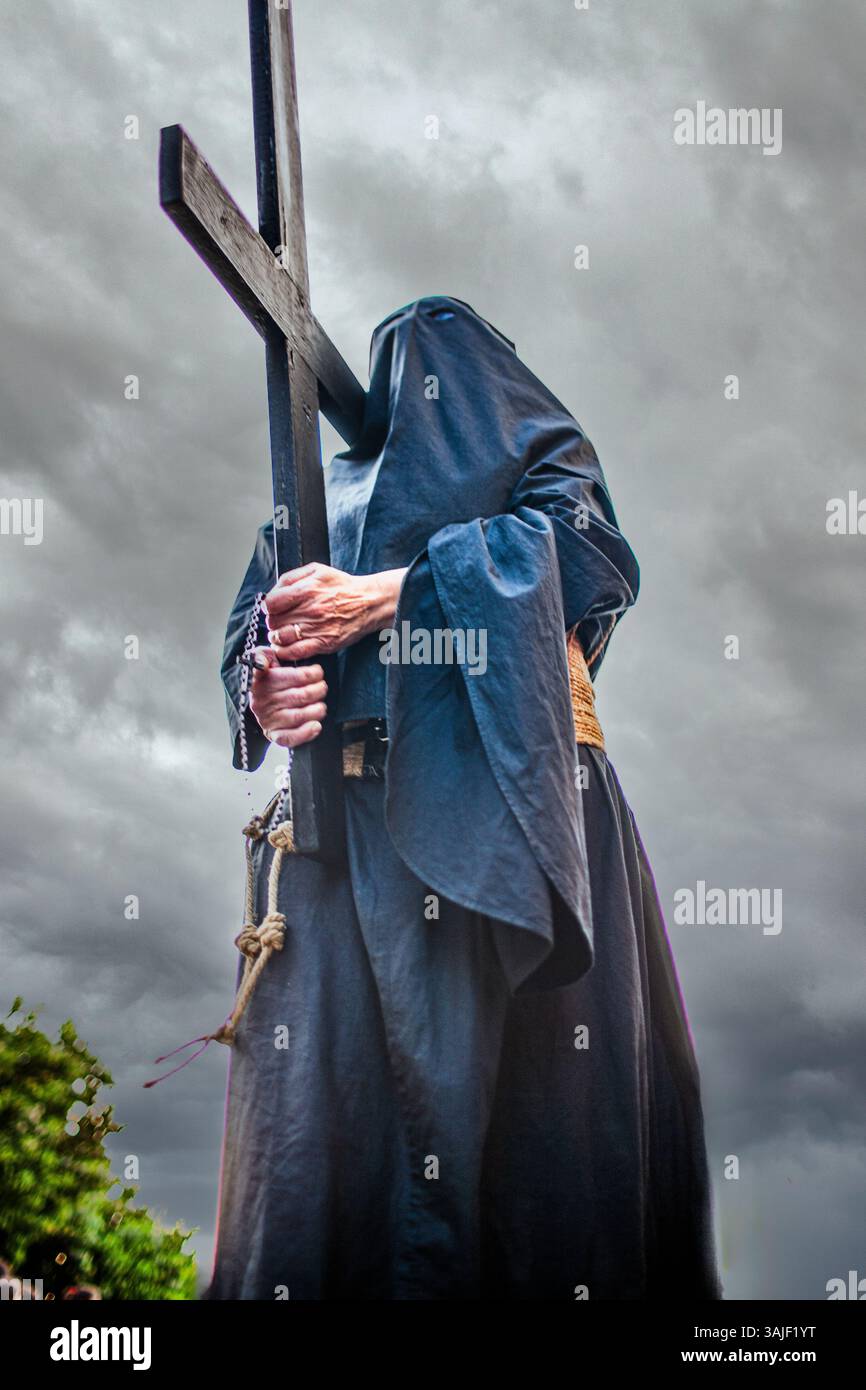 A hooded penitent solemnly carries a wooden cross in Seville ...