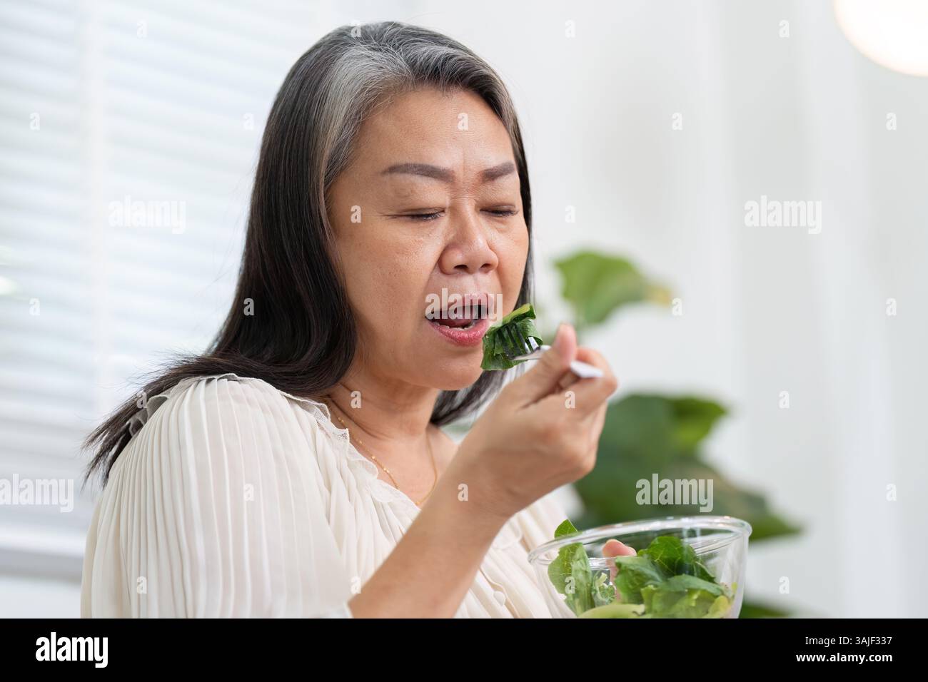 Healthy Eating and Elderly Wellness. An elderly woman enjoying a fresh salad, promoting health ...