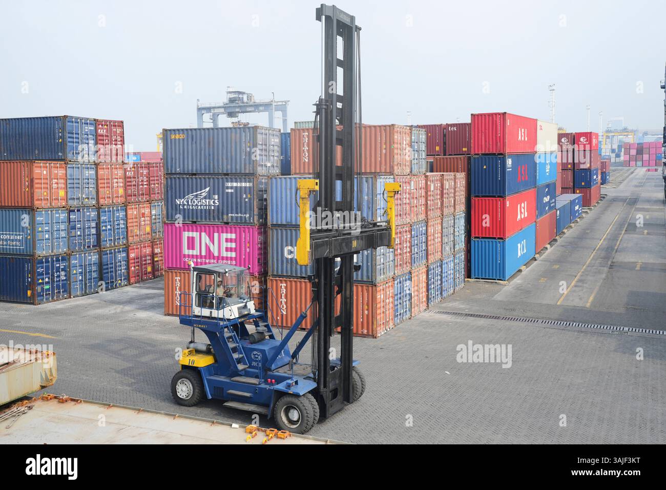 A heavy machine drives past shipping containers stacked at Jakarta ...