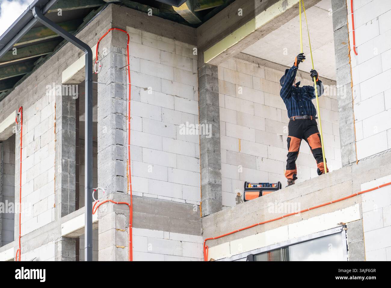 A worker in safety gear carefully measures the height of a wall ...