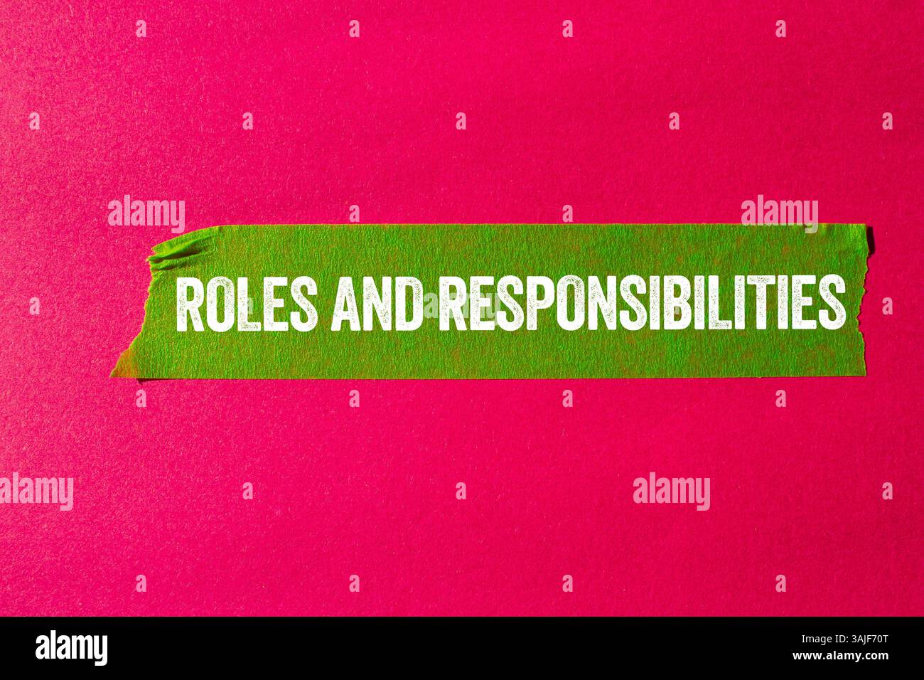Roles and responsibilities message written on ripped torn green paper tape on pink background ...