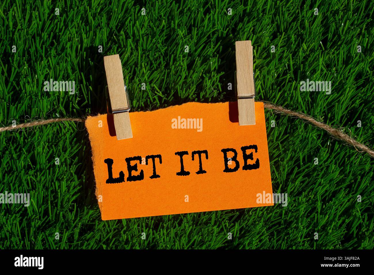 Let it be message written on ripped torn orange paper piece on green ...