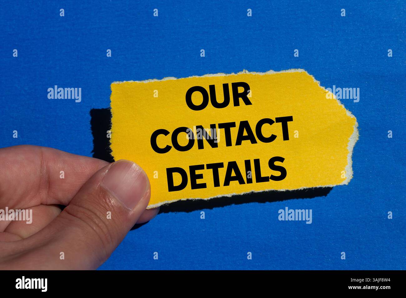 Our contact details message written on ripped torn yellow paper piece on blue background ...