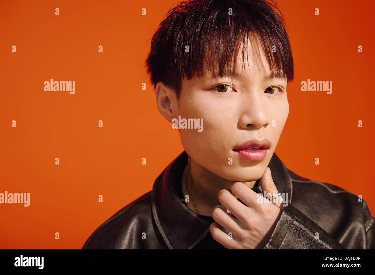 Handsome Asian man poses thoughtfully against a bold orange background ...