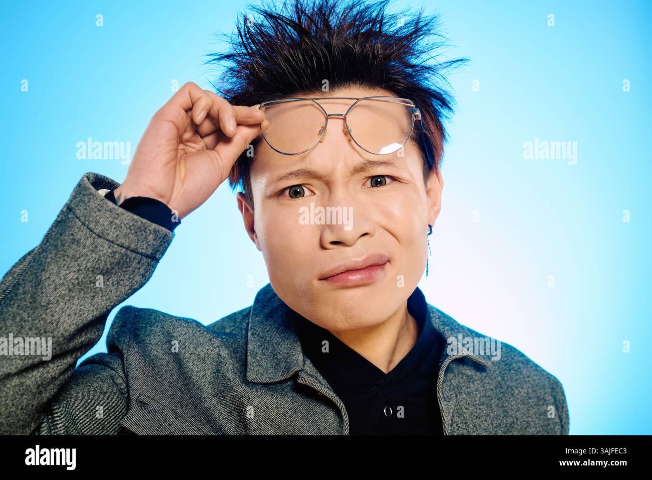 Handsome Asian man displays a curious expression while adjusting his ...