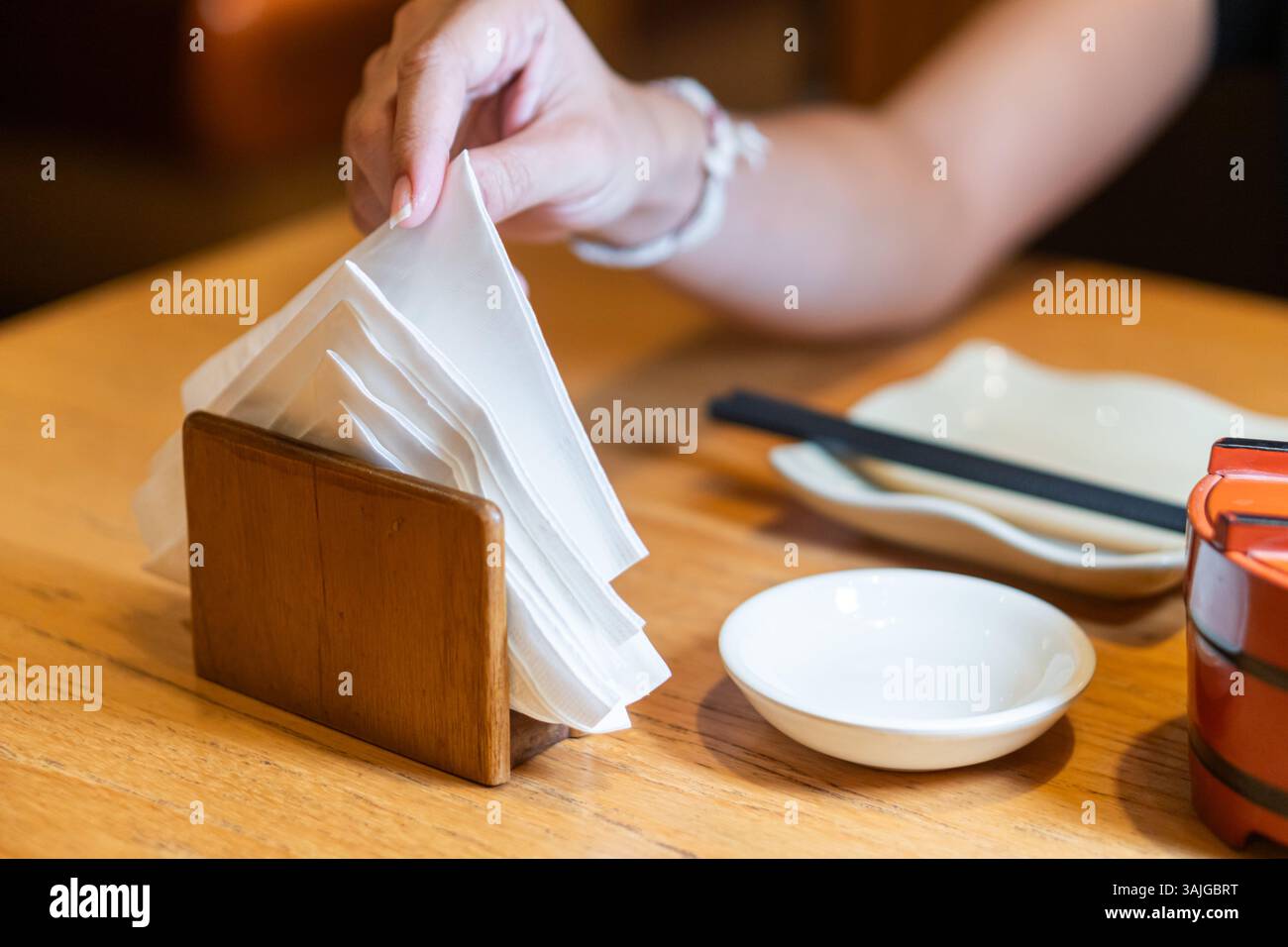A hand holding a stack of napkins in a wooden holder on a restaurant ...