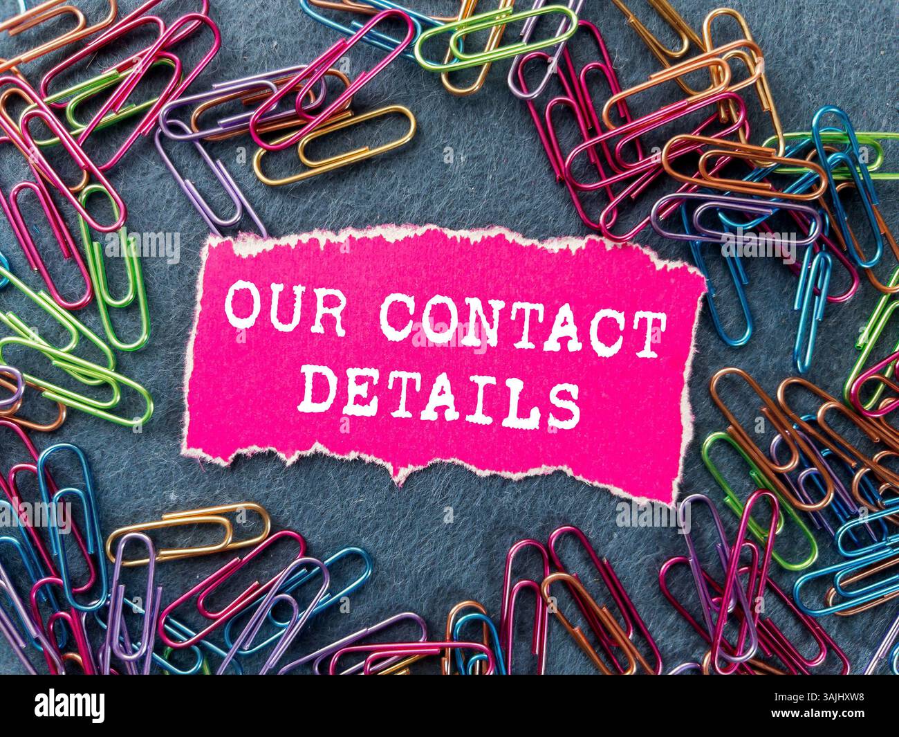Our contact details message written on ripped torn pink paper piece on grey background ...