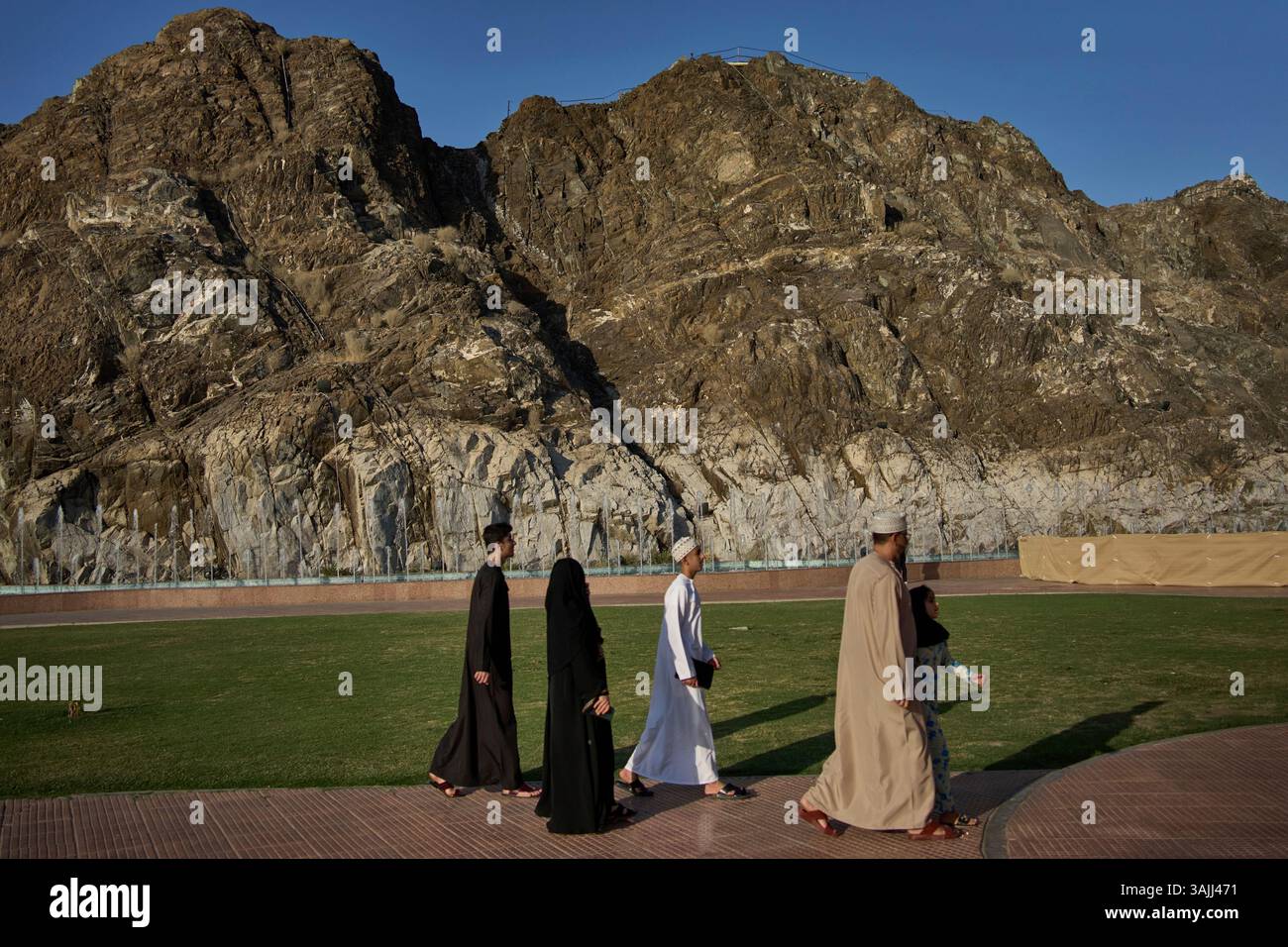 A group of Omani individuals walks in formation along a pathway framed ...