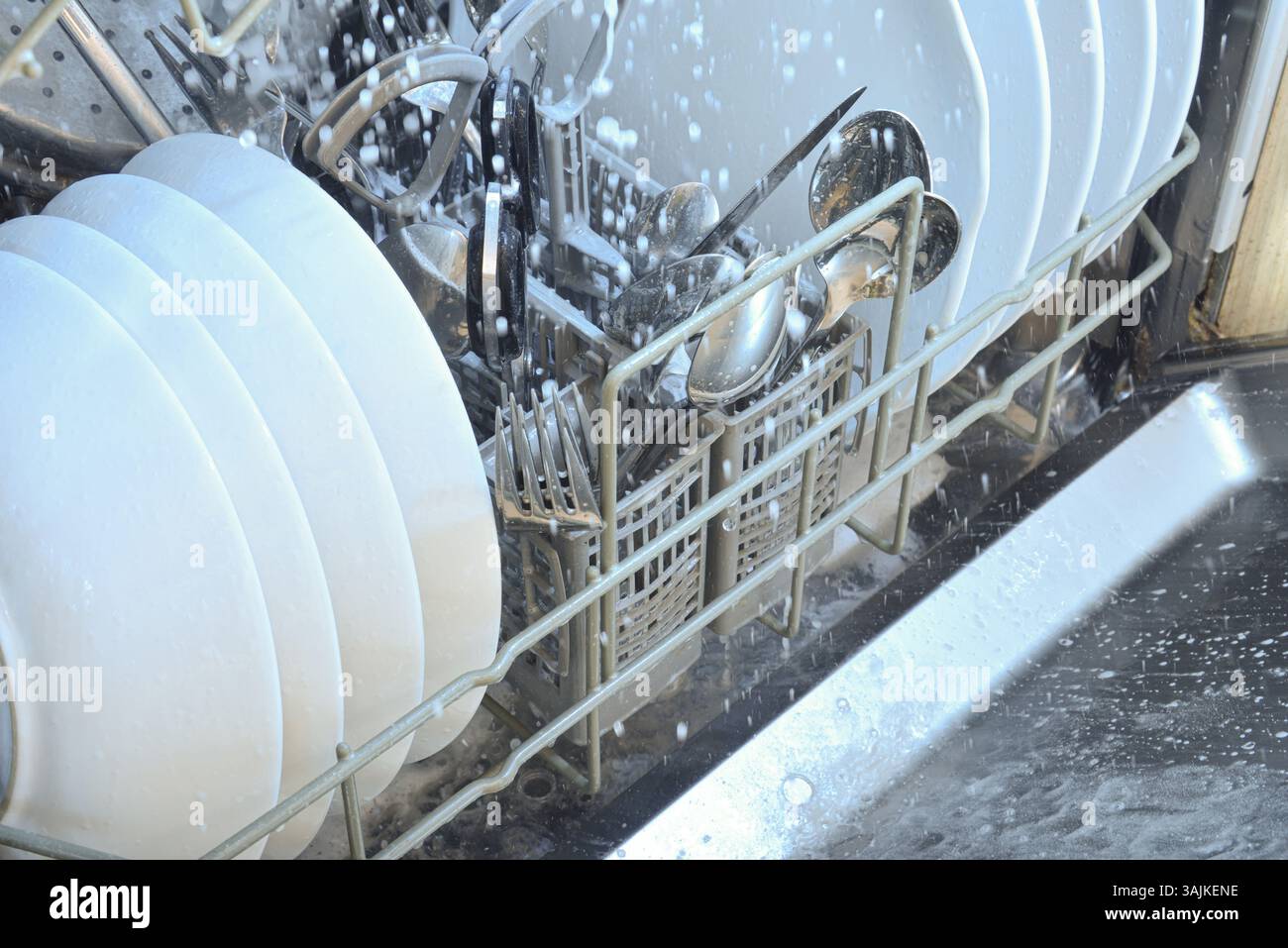 Detail of dishwasher full of plates and cutlery in its basket still ...