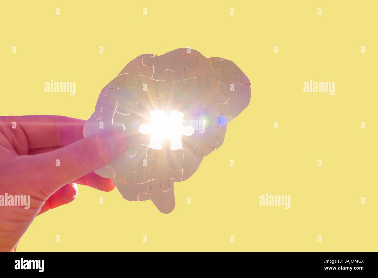 Hand holds a cut-out puzzle piece shaped like a human brain, backlit by ...