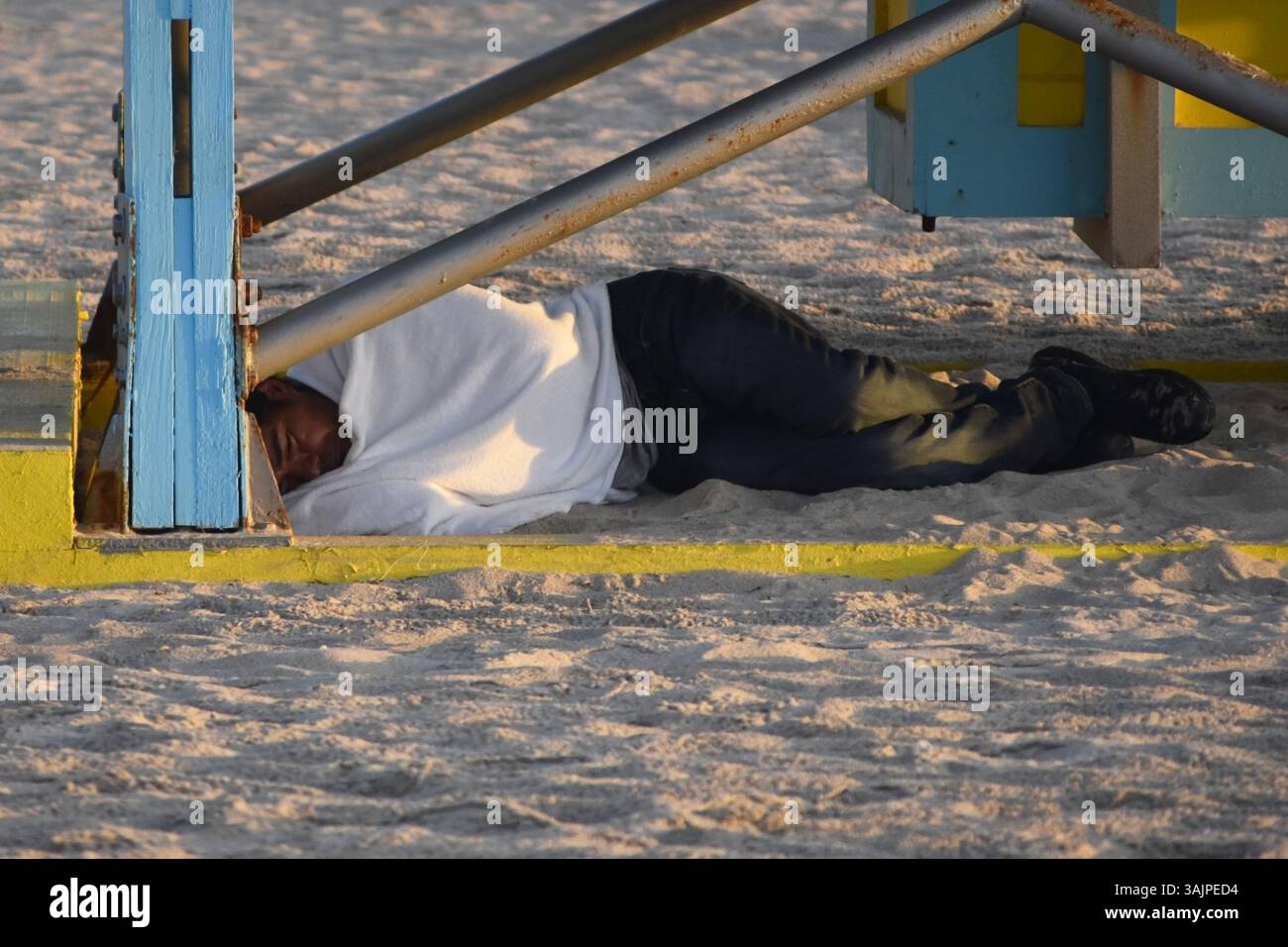 Man lying down on beach in Miami, no shelter, ocean nearby, hot weather ...
