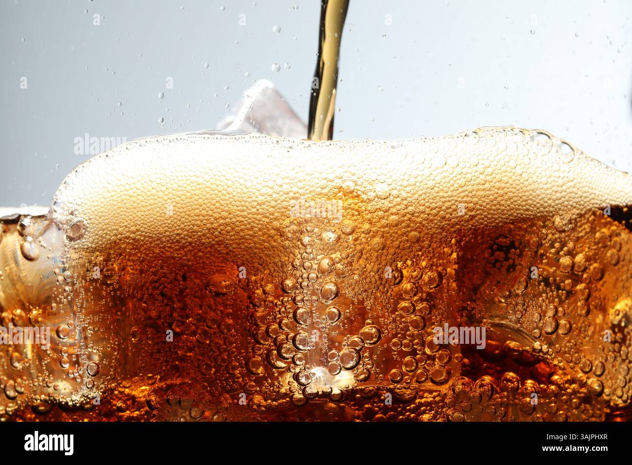 Pouring refreshing cola into glass with ice cubes against light grey background, macro view ...