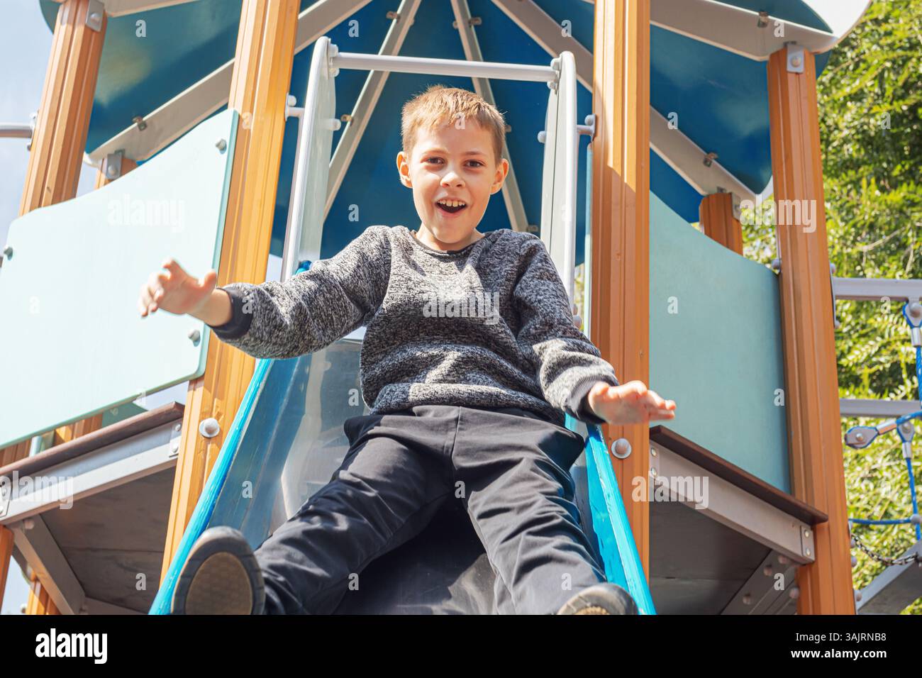 Excited elementary school boy enjoying playground slide with joyful ...