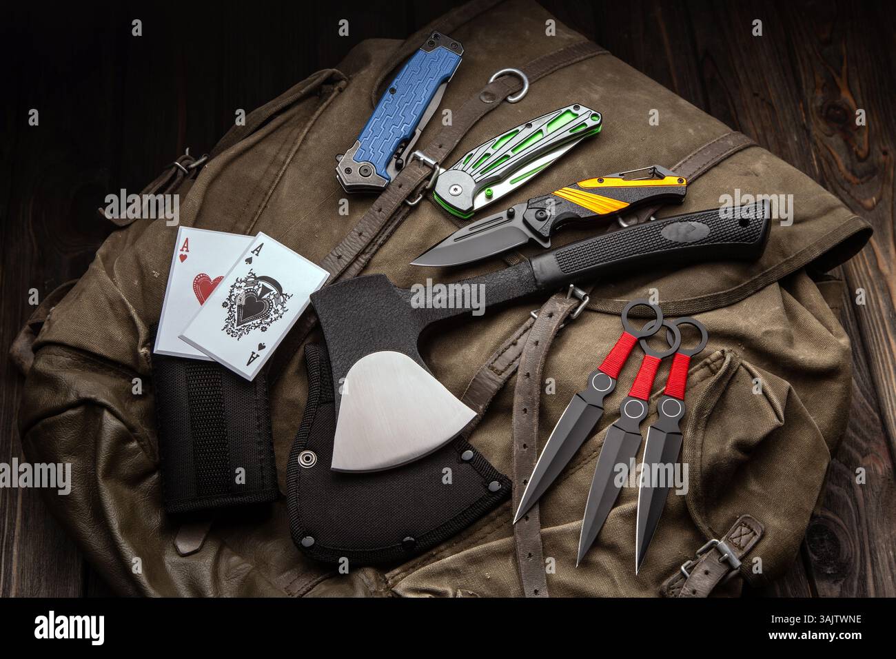Tactical knives, tomahawk, and throwing blades with playing cards on a ...