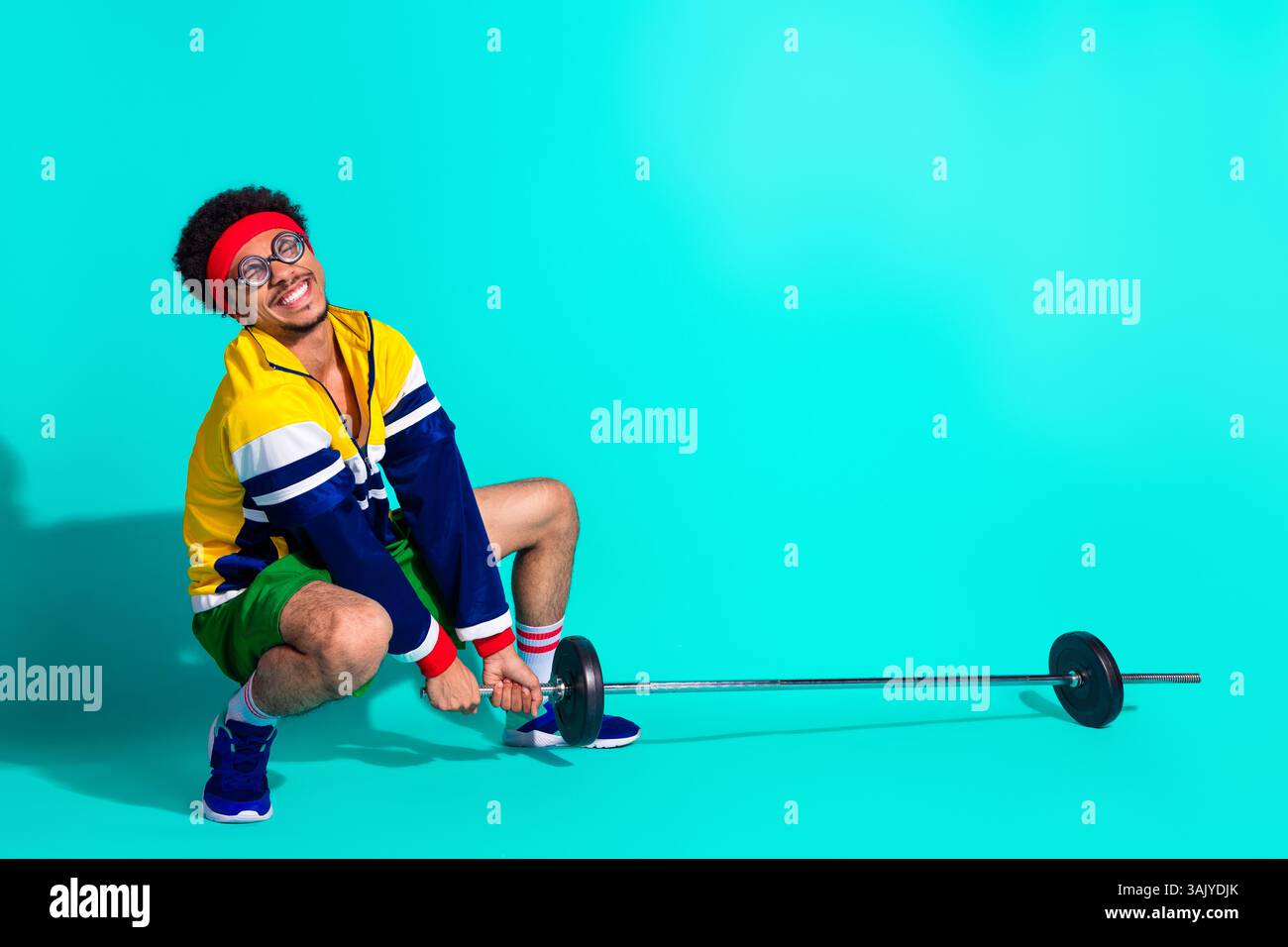 Young cheerful man dressed in retro sportswear lifting barbell on teal ...
