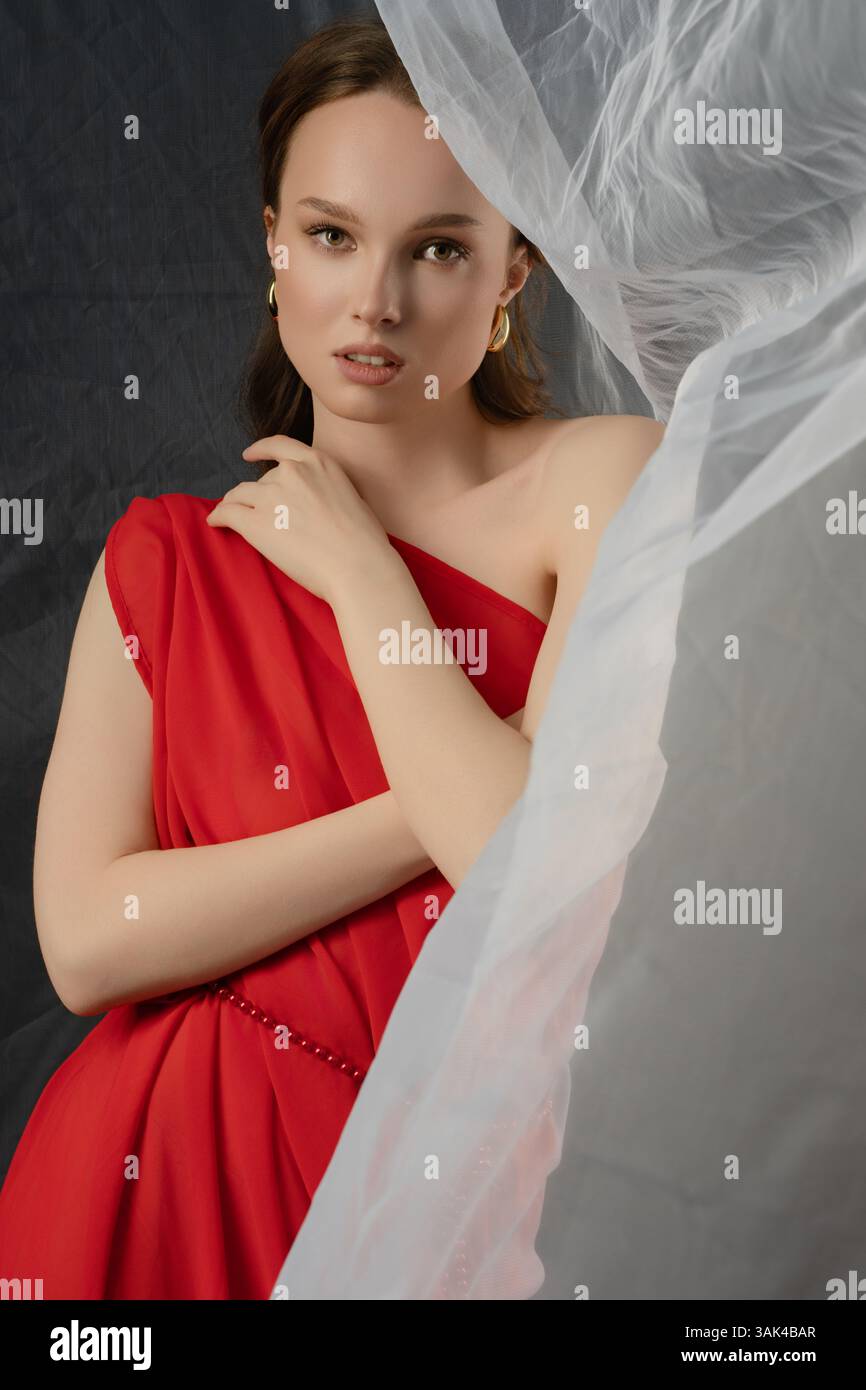 Woman poses in elegant red gown against dramatic studio backdrop ...