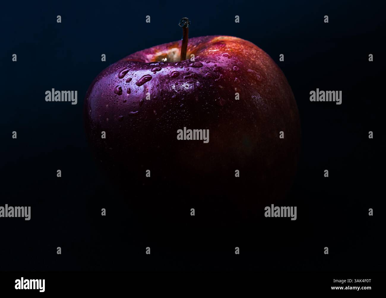 Red apple glistening with droplets of water against a dark background ...
