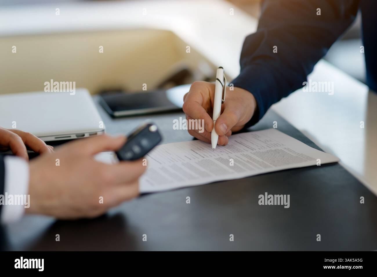 Customer signing contract and salesman holding car keys in a dealership ...