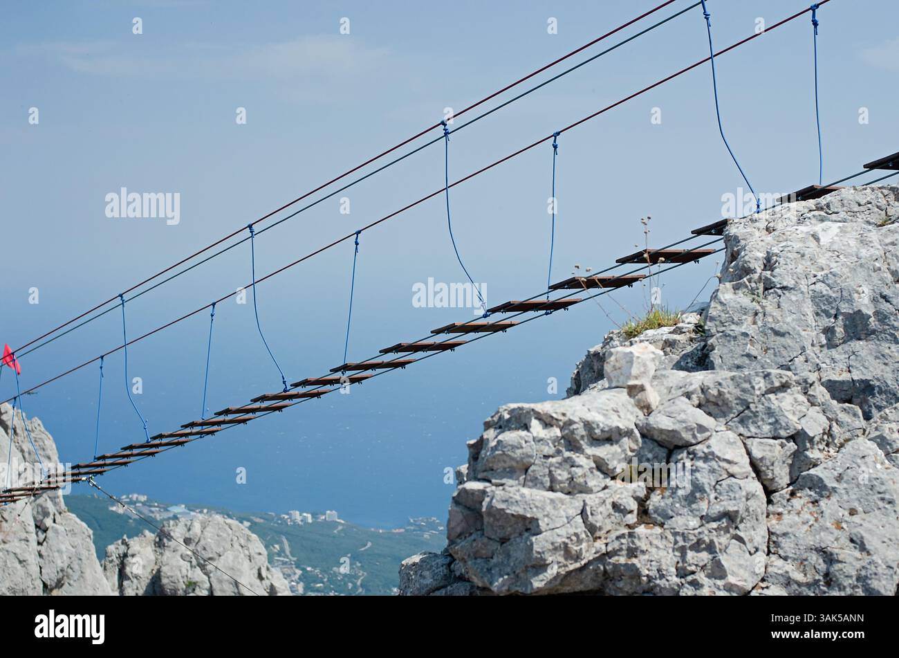 A rope suspension bridge stretches across rugged rocky cliffs, offering ...