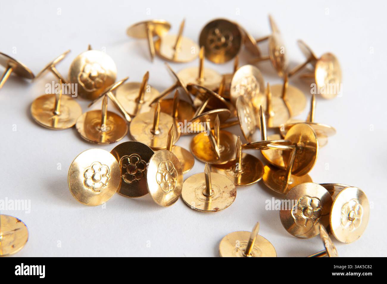 A cluster of gold-colored push pins is displayed on a clean white ...
