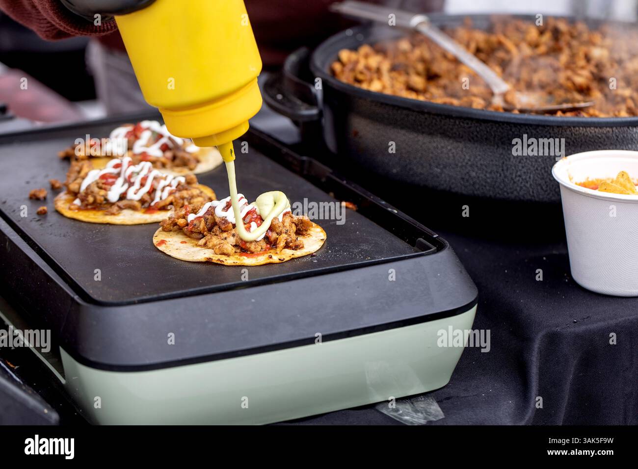 Closeup of chef adding sauce to mini tacos with ground meat. Yellow ...