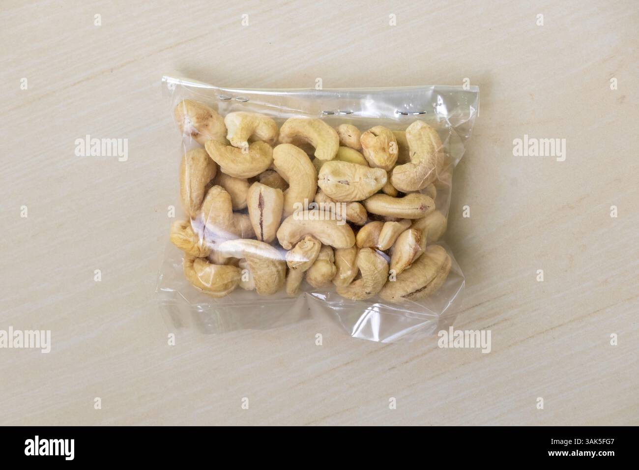 From a top view, a packet of cashew nuts rests on a light wooden ...